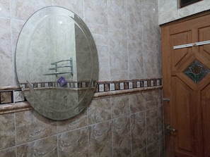 Um banheiro com um espelho grande, uma porta de madeira e um revestimento de azulejos.