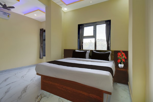 Quarto com cama, janela com cortinas, ventoinha no teto e ar condicionado fixado na parede.