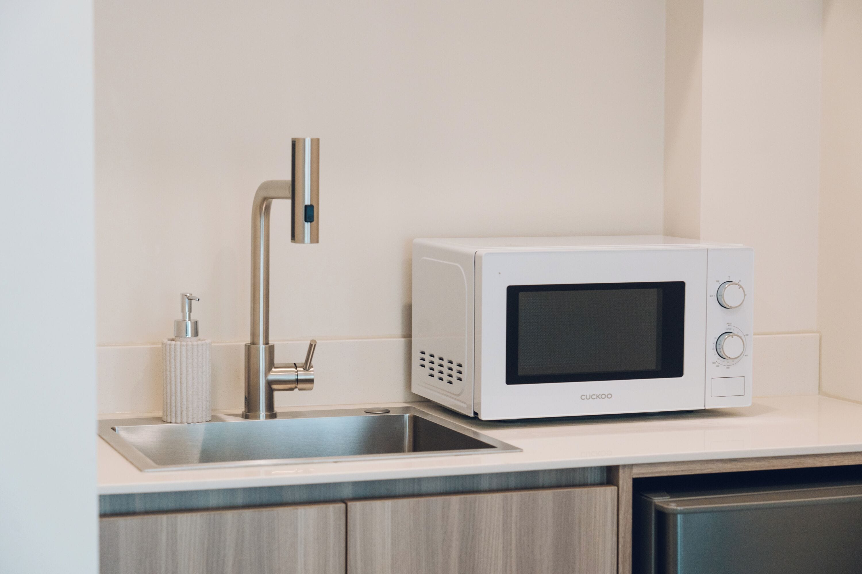 Uma cozinha com micro-ondas branco, pia de aço inoxidável e dispensador de sabonete.