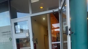 Entrada de um hotel com portas de vidro, piso ladrilhado e parede cor verde-água.