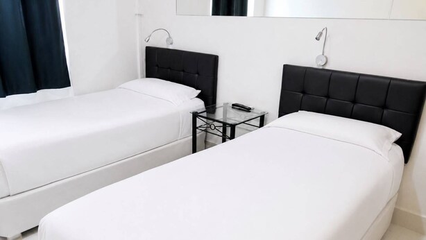 Quarto de hotel com duas camas de solteiro, uma mesinha e um espelho sobre as camas.