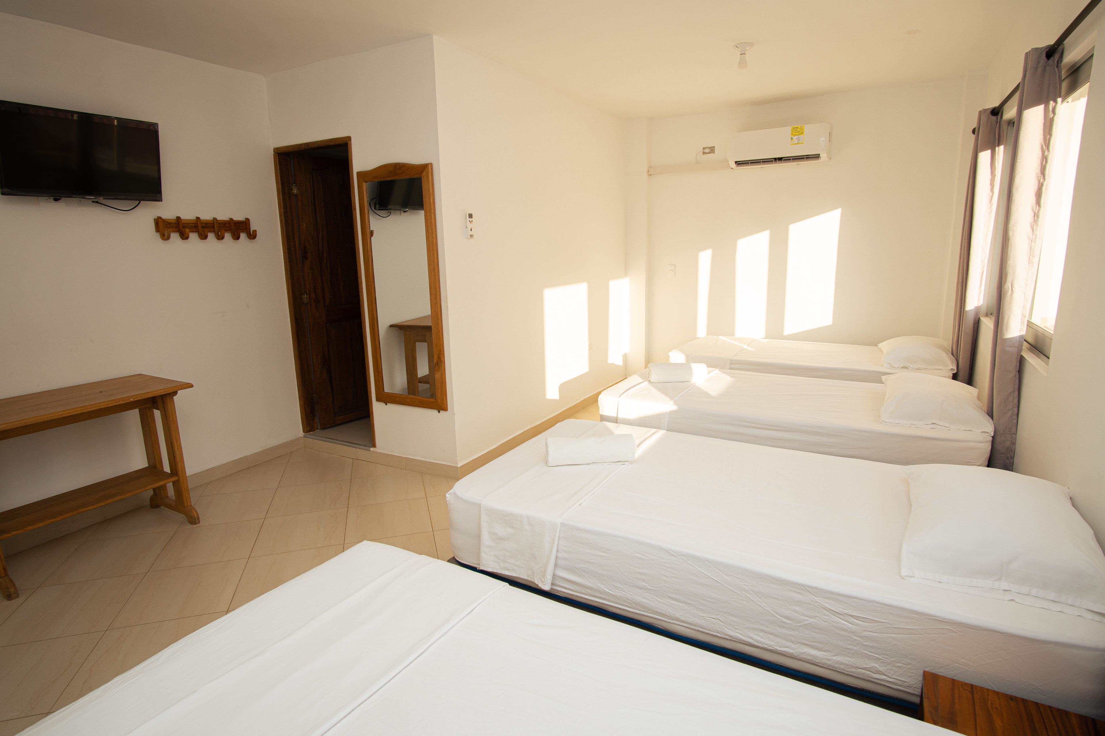 Quarto de hotel com duas camas de solteiro, um banco de madeira, televisão e espelho.