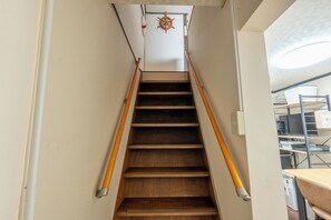 Uma escadaria de madeira com decoração de leme no topo, que dá acesso a um quarto com escrivaninha e estantes.