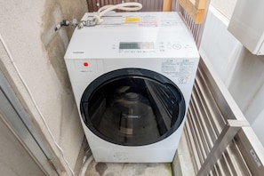 Uma máquina de lavar compacta, branca, com visor digital, painel de controle e uma porta grande preta.