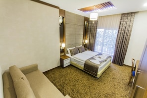A hotel room with a large bed, a sofa, a nightstand, and a window with curtains.