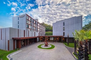 Um hotel com fachada moderna, um pátio central com uma escultura, e uma placa com a inscrição 'CROWE PLAZA'.
