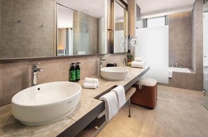 Uma casa de banho moderna com um espelho grande, duas pias, uma banheira e um lavatório com um porta-toalhas.