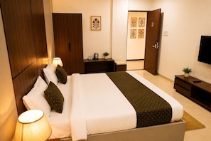 Quarto de hotel com cama, luminárias de cabeceira, mesa de apoio, televisão e uma porta que dá para outro quarto.