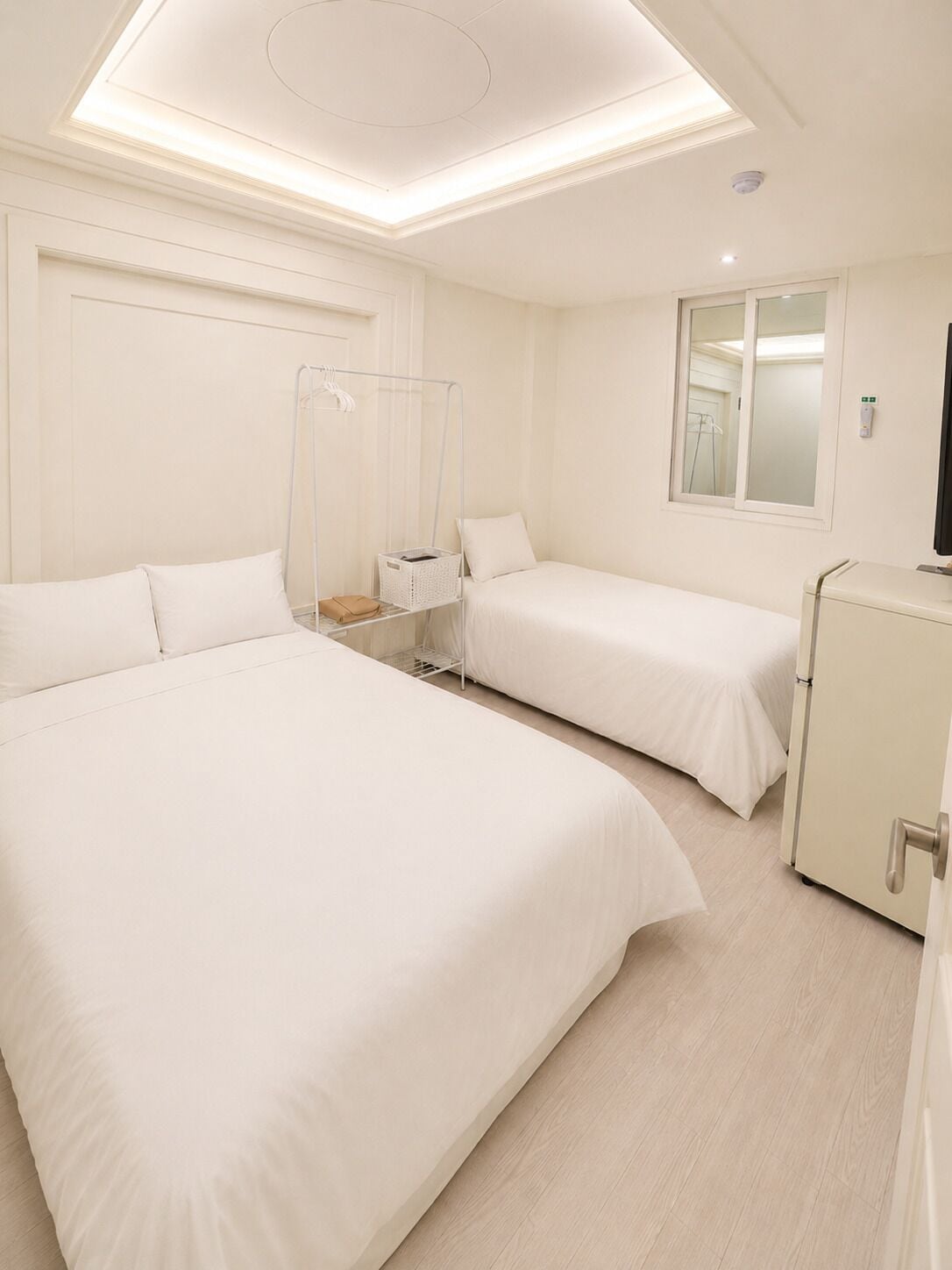 Quarto de hotel com duas camas, mesa de cabeceira, guarda-roupa e luminária no teto.