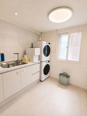 Cozinha moderna com máquina de lavar e secar integradas, pia e janela com persianas.