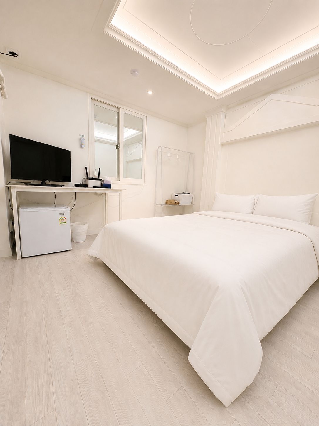 Quarto de hotel com cama, televisão, escrivaninha e pequeno frigorífico.
