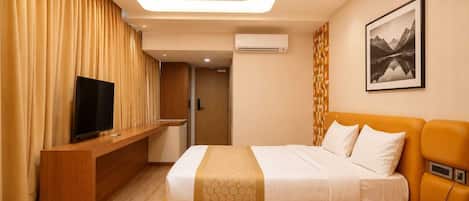Quarto de hotel com cama, televisão, secretária e telefone.