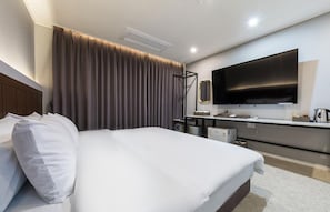 Quarto de hotel moderno com uma cama grande, uma TV de tela plana na parede, uma mesa com cadeira e uma janela com cortinas.