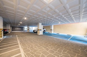 Um parque de estacionamento com vários níveis, design geométrico no teto, sinalização clara e uma combinação de espaços de estacionamento abertos e cobertos.