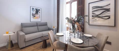 Uma sala de estar moderna com um sofá cinzento, uma mesa de jantar posta para dois e obras de arte nas paredes.