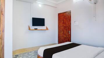 Quarto com cama, televisão na parede, porta de madeira e ventoinha no teto.