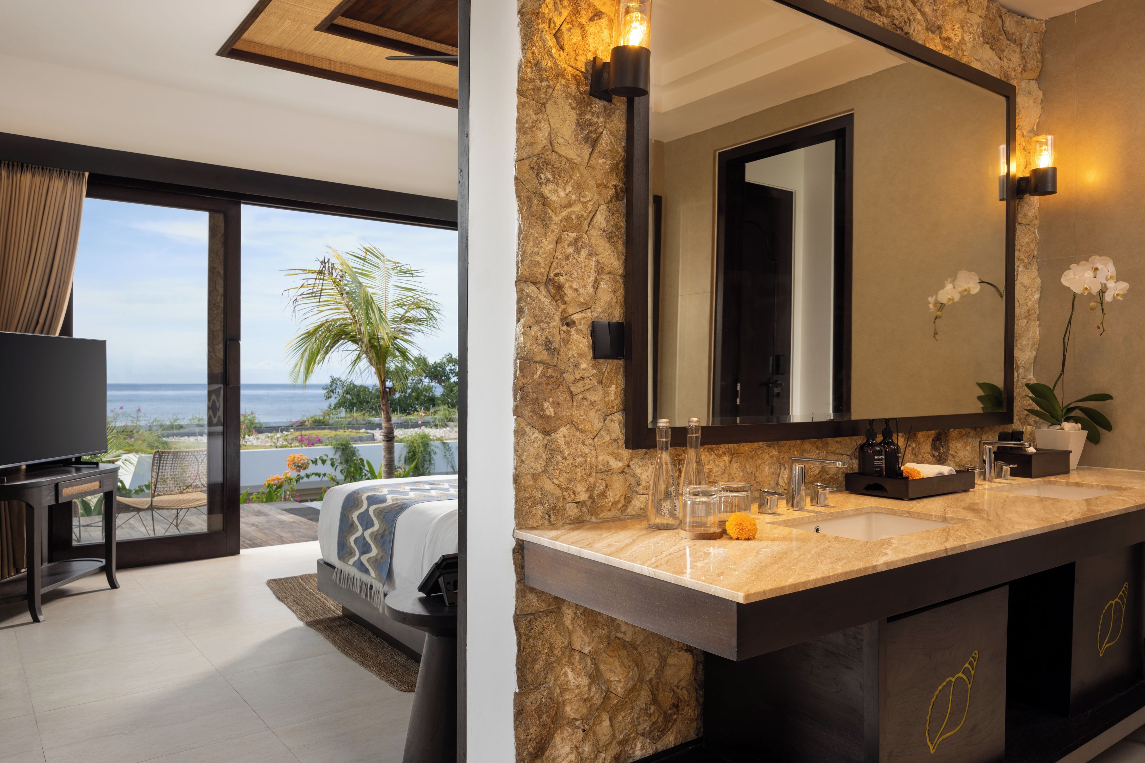 Casa de banho moderna com um espelho grande, bancada de mármore e vista para o oceano.