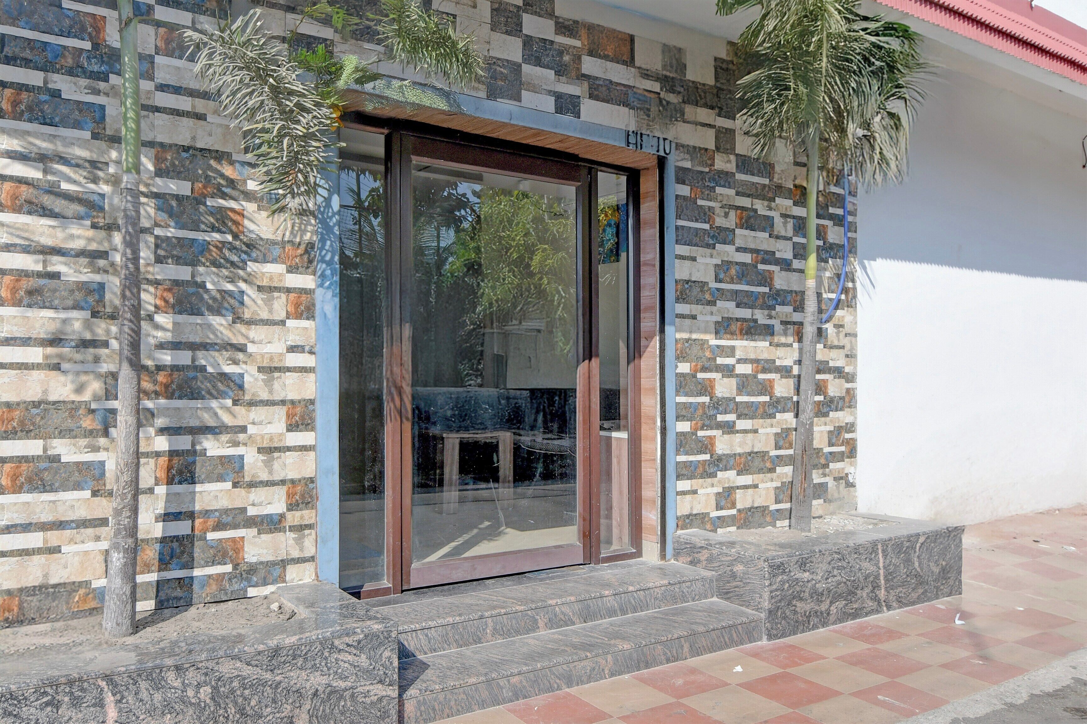 Entrada de um edifício com porta de vidro, parede de pedra e degraus que levam à porta.