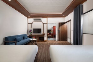 Quarto de hotel com sofá, uma mesinha com um vaso, televisão e armário de madeira.