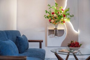 Uma sala de estar moderna com um sofá azul, uma mesa de centro de vidro e um vaso fixado na parede com flores.