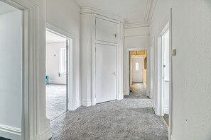 Um corredor com paredes brancas, piso coberto por carpete e uma porta que dá para outro cômodo.