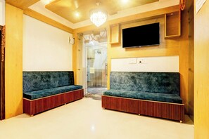 Um quarto com dois sofás verde-escuros, uma televisão de tela plana na parede e um lustre.