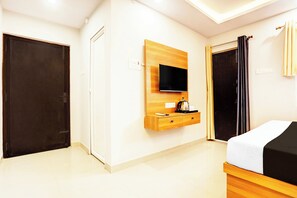 Quarto de hotel com cama, televisão na parede, cômoda de madeira e uma porta.