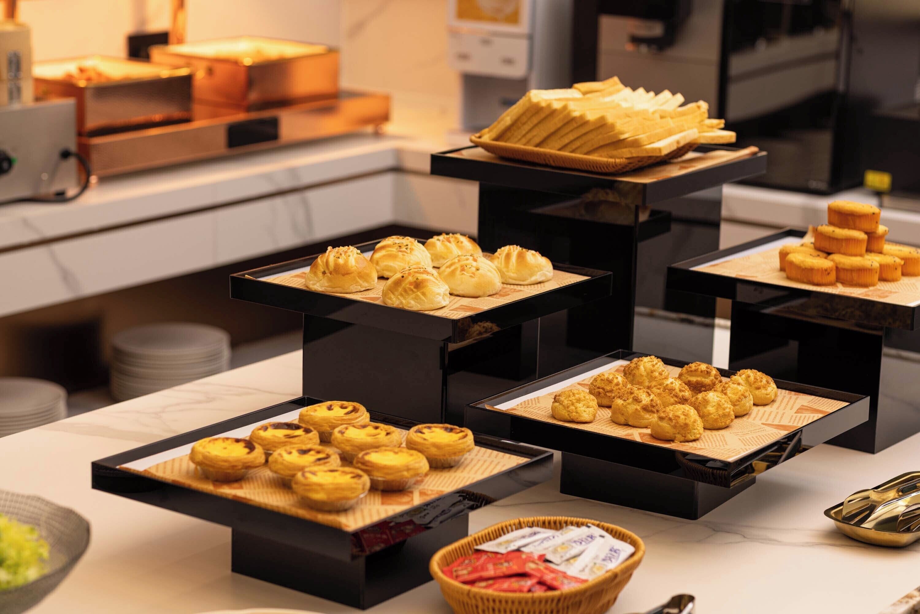 Buffet com diversos produtos de panificação expostos em suportes pretos.