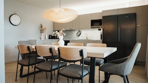 Uma cozinha moderna com área de jantar, com uma mesa redonda, seis cadeiras, uma geladeira preta e um lustre.