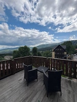 Um deck de madeira com mobiliário externo, com vista para uma paisagem montanhosa e uma aldeia.