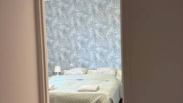 Quarto com cama, mesa de cabeceira e parede com padrão de folhas.