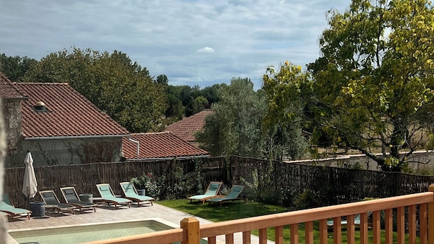 Uma área de piscina com um deck de madeira, espreguiçadeiras e um edifício de pedra ao fundo.