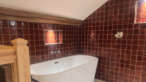 Um banheiro moderno com uma banheira independente, paredes revestidas de azulejos escuros e piso de madeira.