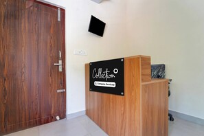 Uma área de recepção com uma mesa de madeira, uma placa indicando ser um local de serviço da empresa, e uma porta de madeira fechada.