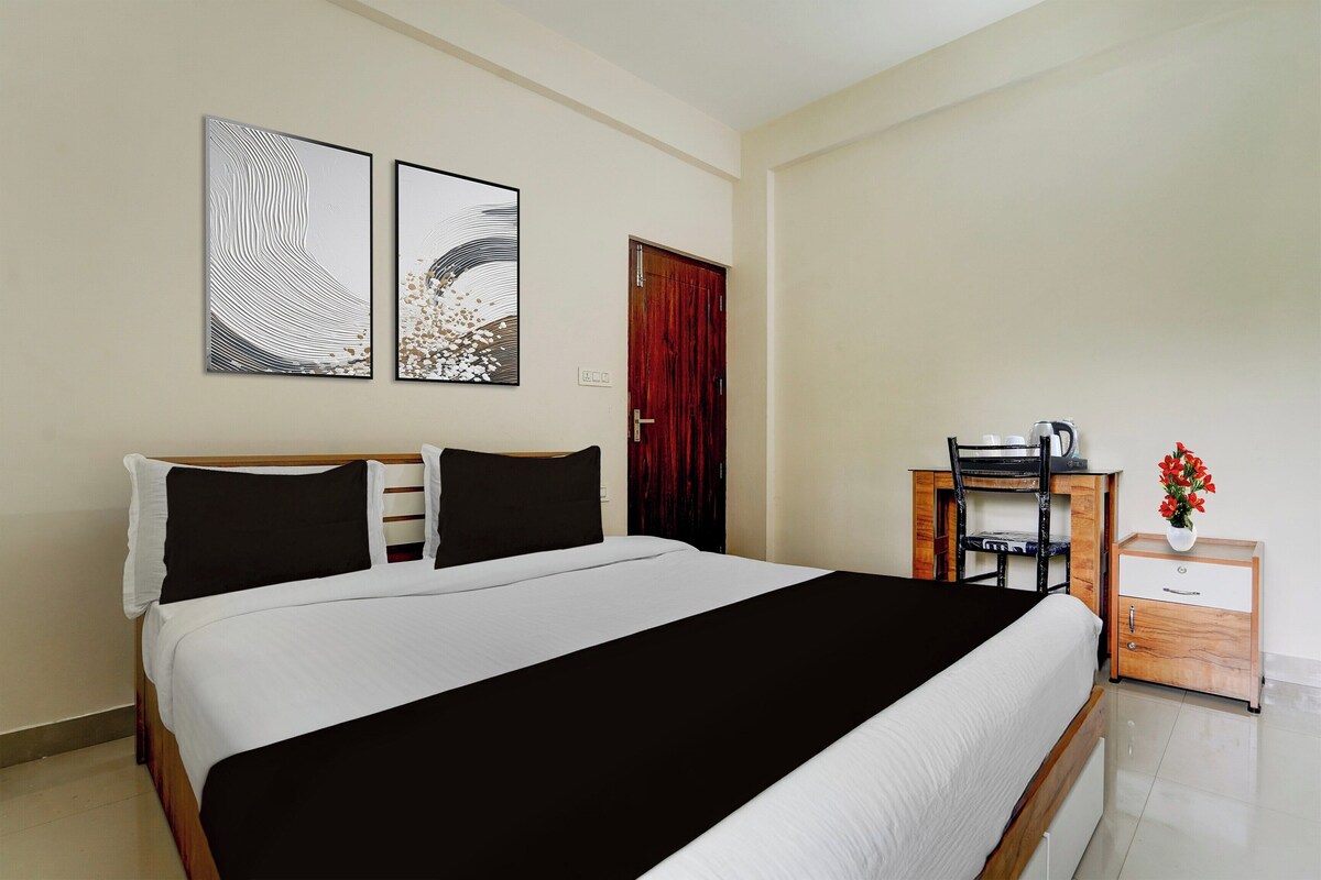 Quarto de hotel com cama, mesa de cabeceira de madeira, escrivaninha e duas obras de arte penduradas na parede.