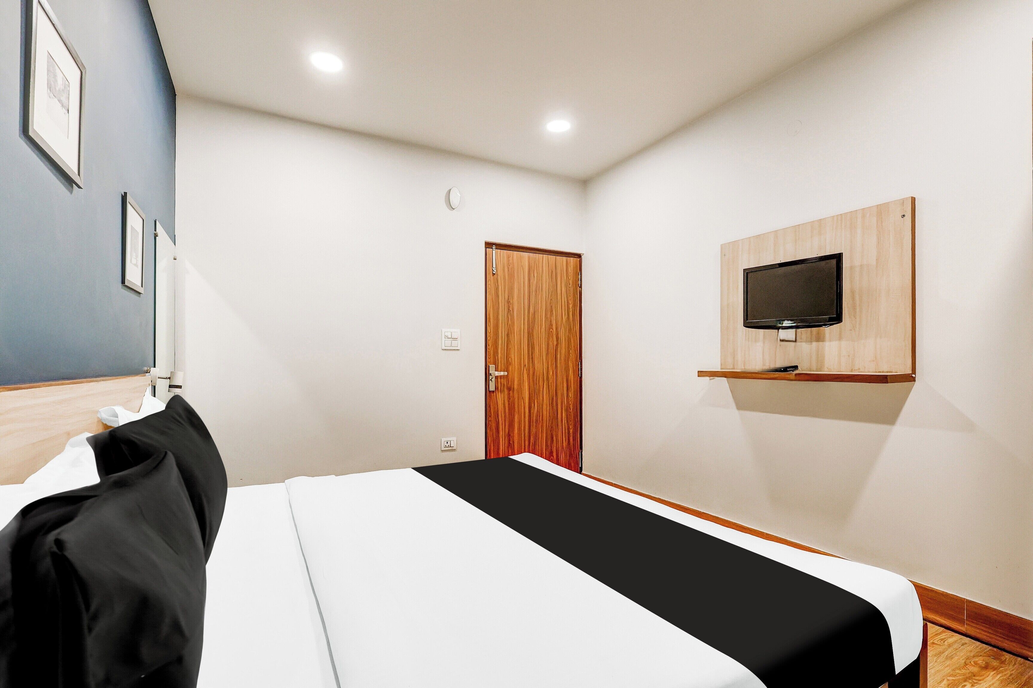 Quarto de hotel com uma cama, uma televisão presa à parede e uma porta de madeira.