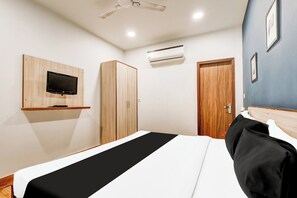 Quarto de hotel com cama, televisão fixada na parede, guarda-roupa, ar condicionado e porta.