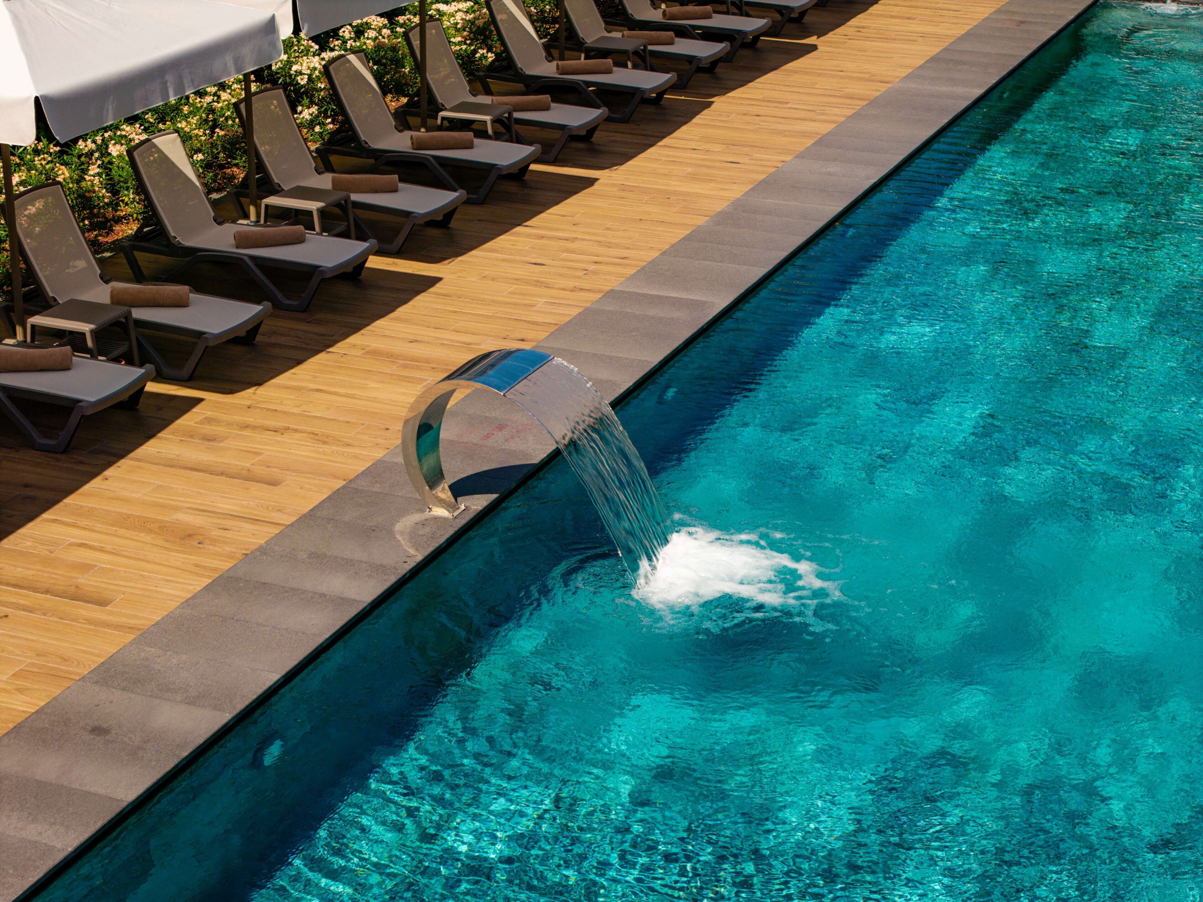 Piscina com um elemento aquático, rodeada por espreguiçadeiras e guarda-sóis.