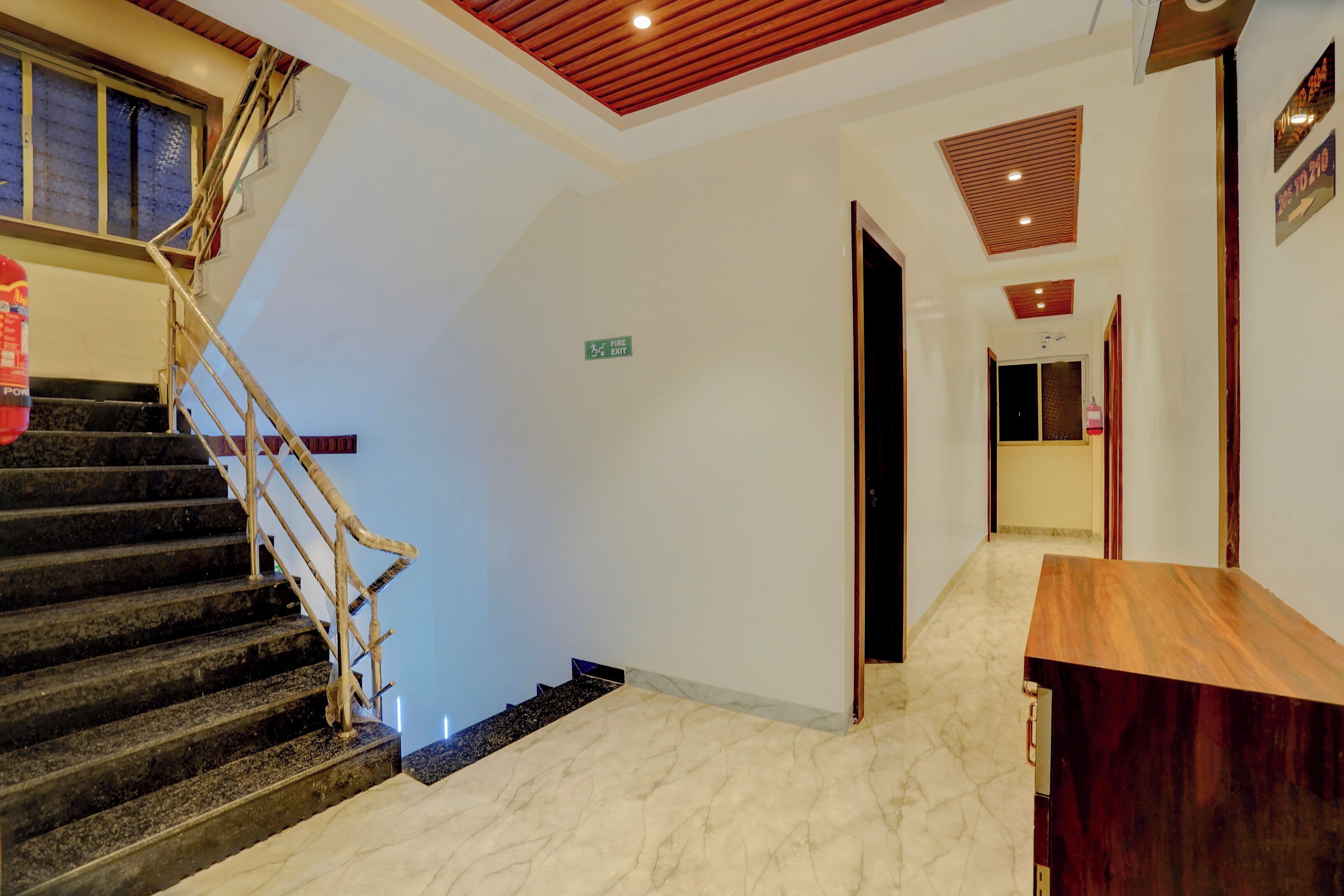 Um hall de hotel com piso de mármore, escada de madeira e placa de saída de incêndio.