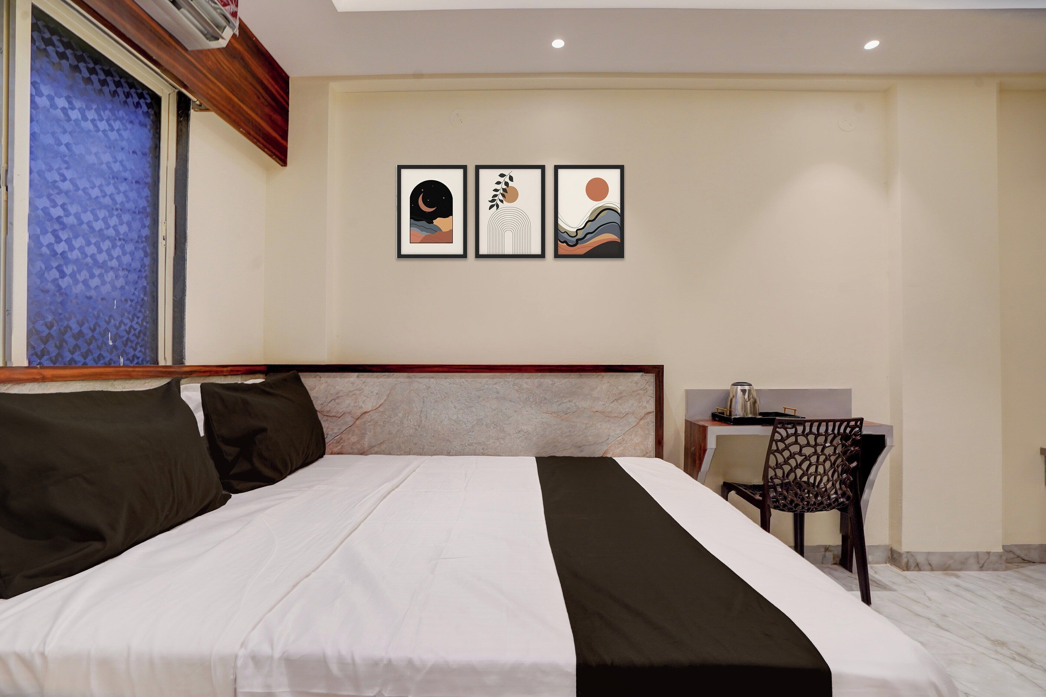 Quarto de hotel com cama, escrivaninha e uma cadeira. Três obras de arte emolduradas na parede.