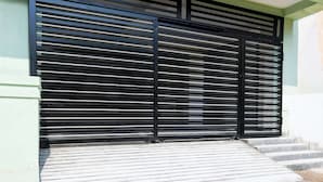 Um portão de metal preto grande, com ripas horizontais, dá acesso a um conjunto de degraus de concreto.