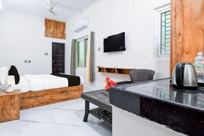 Quarto de hotel com cama, escrivaninha, cadeira, televisão e janela com cortinas.
