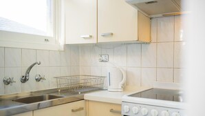 Uma cozinha com armários brancos, uma pia de aço inoxidável, uma chaleira e um fogão.