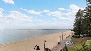 Uma praia com um calçadão pavimentado, postes de luz e vista distante do mar.
