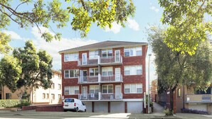 Um edifício residencial de vários andares com fachada de tijolos, varandas e uma carrinha branca estacionada em frente.