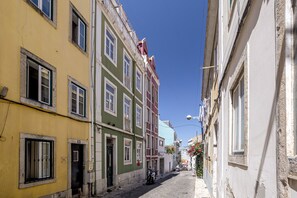 Uma rua de paralelepípedos estreita, ladeada por edifícios coloridos, uma motocicleta estacionada e um céu azul claro.