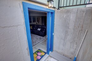 A narrow stairway leading to a room with a blue door, a patterned rug, and a dark-colored sofa.