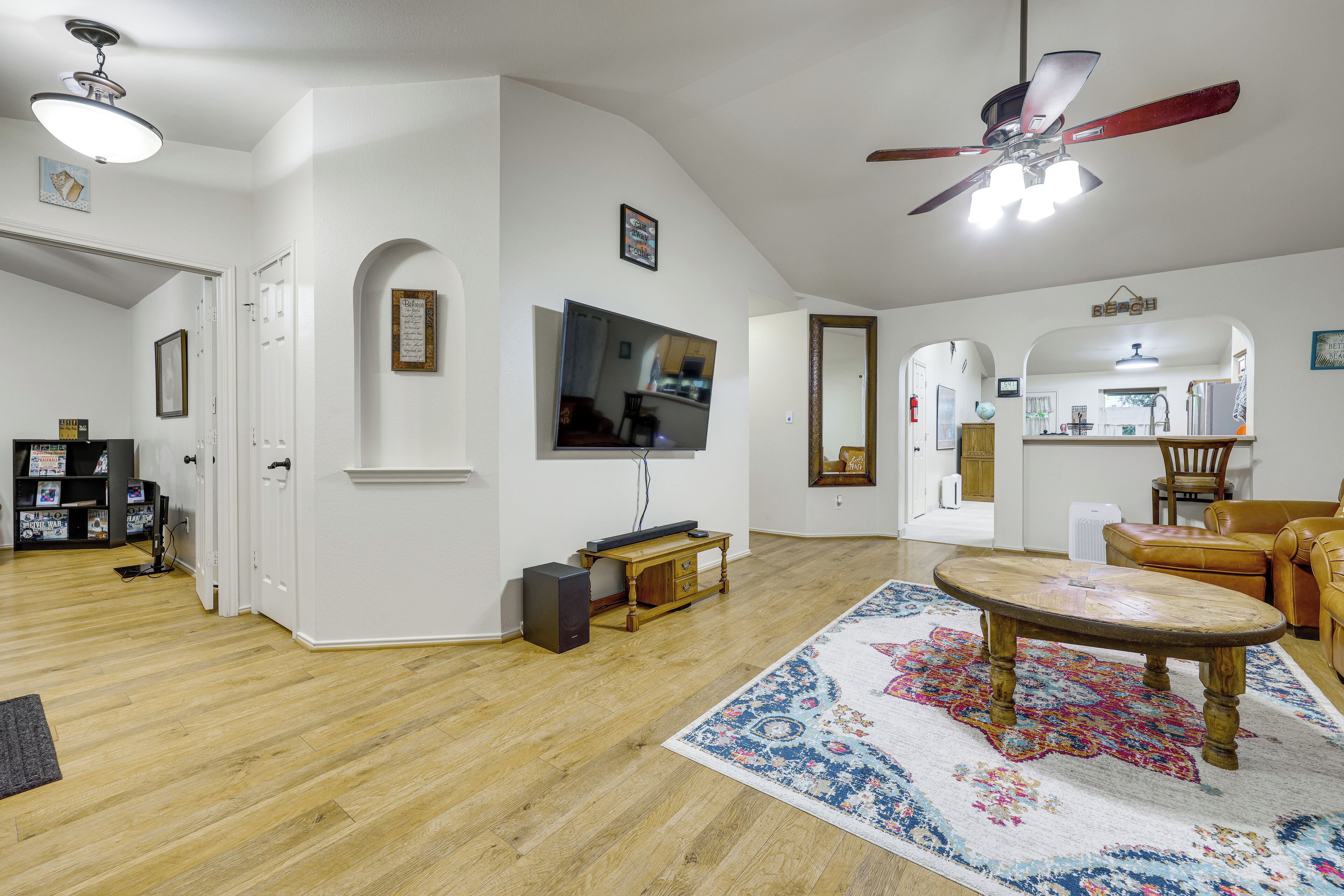 Uma sala de estar espaçosa com piso de madeira, ventilador de teto, televisão de tela plana e área de jantar com mesa e cadeiras.