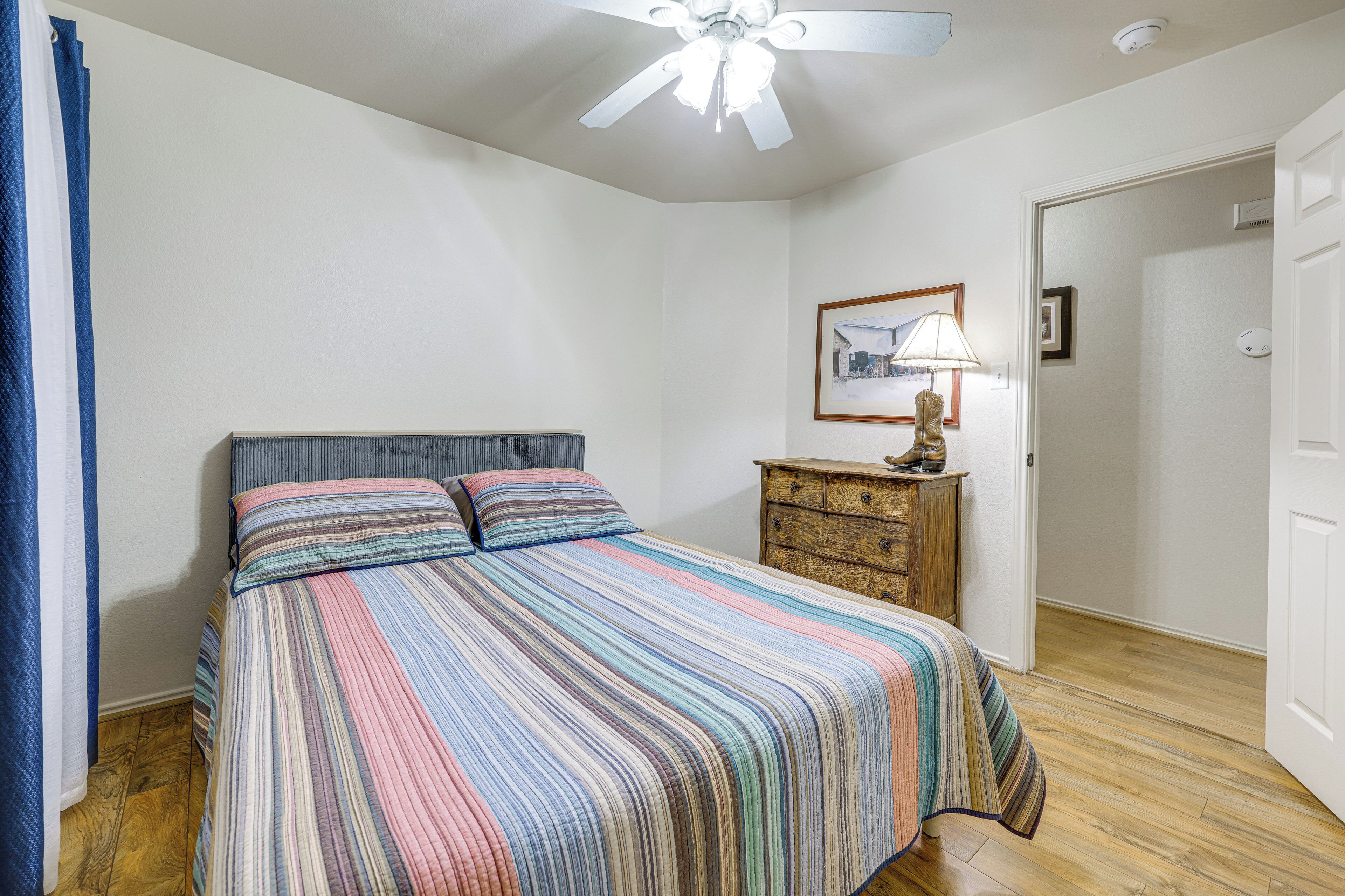 Quarto com cama, cômoda, ventoinha no teto e porta.