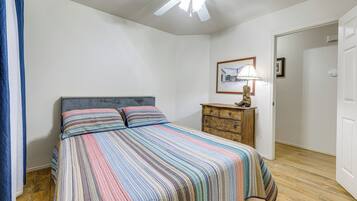 Quarto com cama, cômoda, ventoinha no teto e porta.